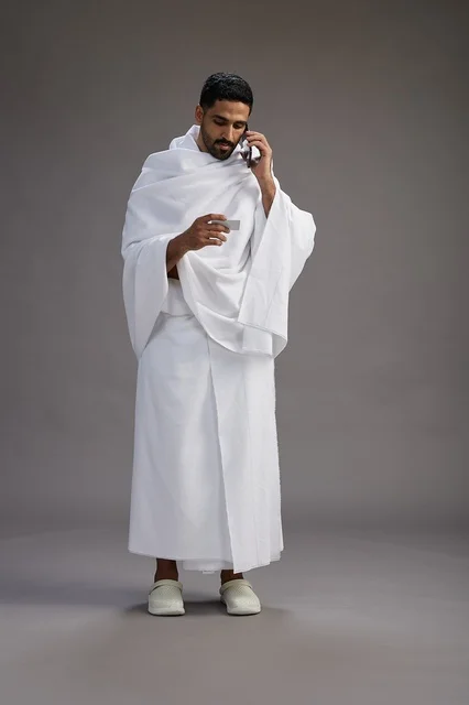 A portrait of a Saudi man in Ihram clothing holding a blank white card ...