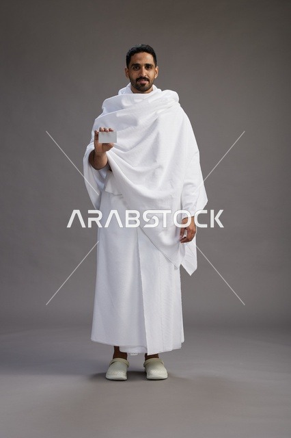 A portrait of a Saudi man in Ihram clothing holding a blank white card ...
