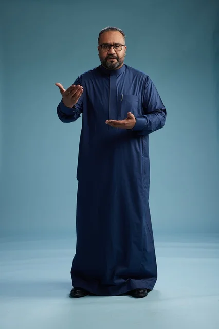 A portrait of a Saudi man standing wearing a navy blue thobe looking at ...