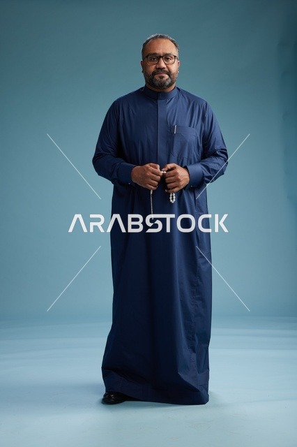 A portrait of a Saudi man standing wearing a navy blue thobe looking at ...