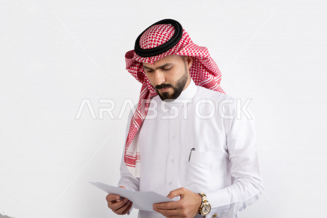 Portrait of a young Arab, Gulf cultured man standing and reading notes ...