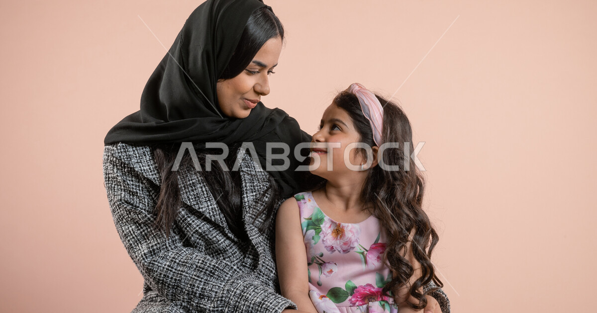 Portrait of a Saudi Arabian Gulf girl sitting next to her mother with ...
