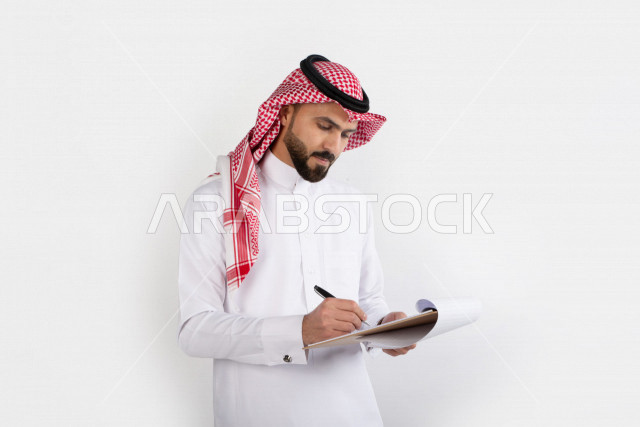 Portrait, Saudi Arabian businessman standing and writing in a folder ...