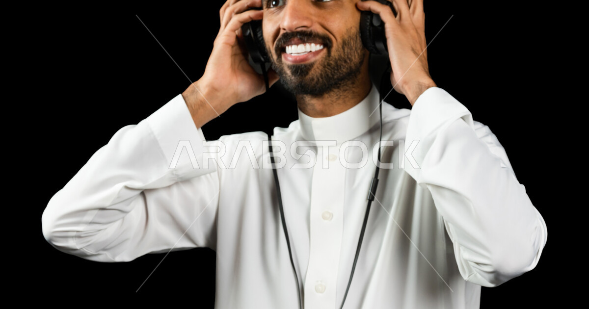 A Saudi Arabian Gulf man puts a headset on his ear, listening to music ...
