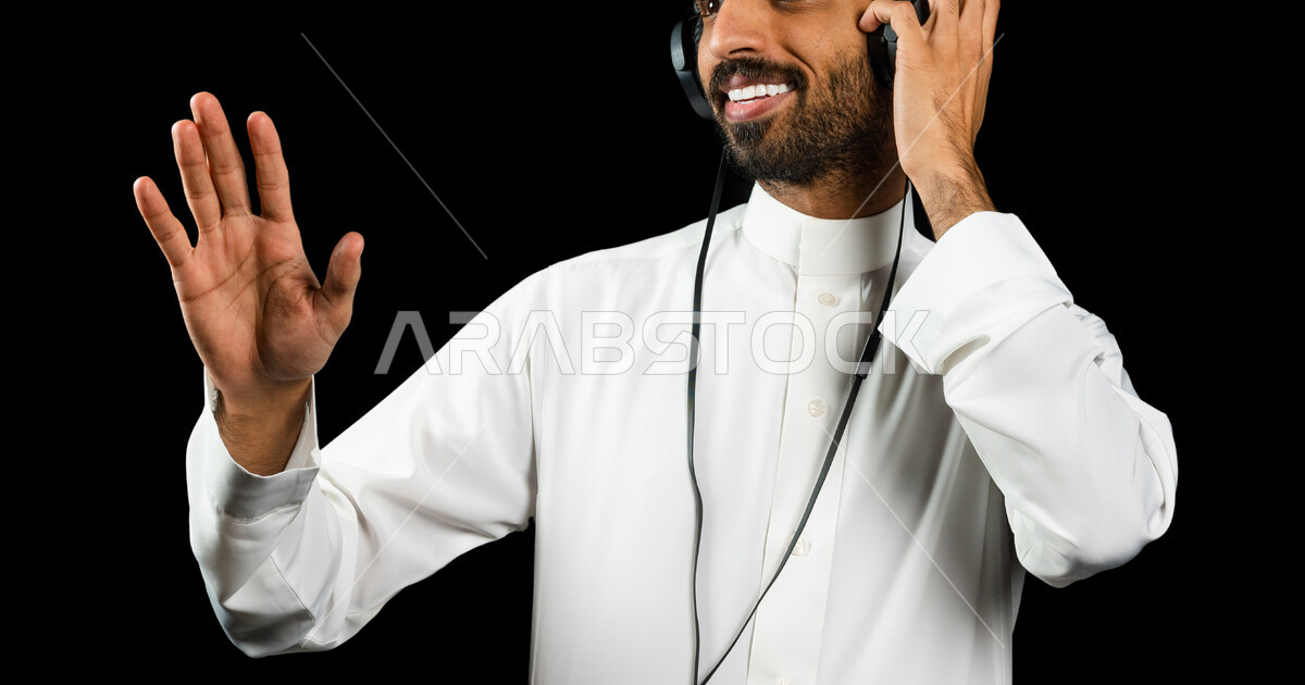 A Saudi Arabian Gulf man puts a headset on his ear, listening to music ...