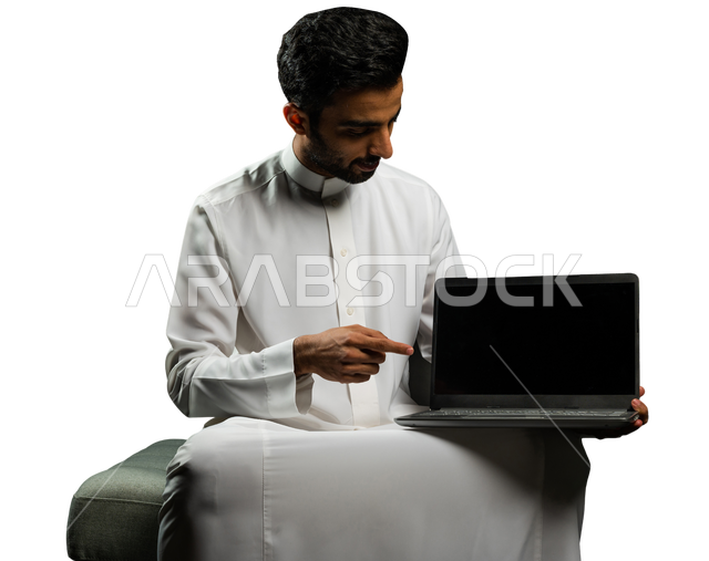 A Saudi Arabian Gulf man wearing a Saudi dress, using a laptop computer ...