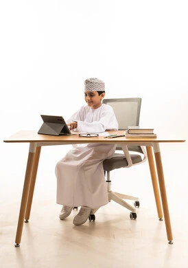 Saudi Boy in Traditional Thobe Using Tablet at Desk - Photo