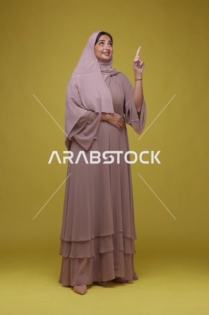 Saudi Woman in Abaya Pointing Up on Yellow Background - Photo