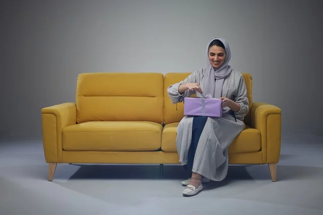 Saudi Woman on Yellow Sofa Holding Purple Gift Box - Photo