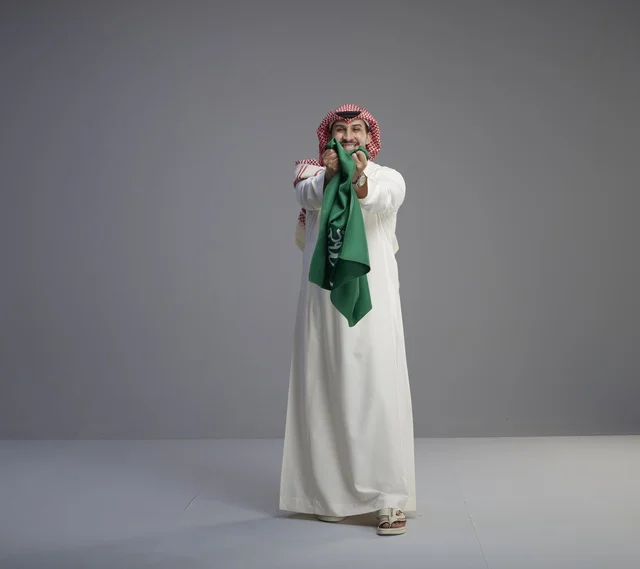 رجل سعودي بالزي التقليدي يحمل العلم الوطني في الاستوديو - صورة
