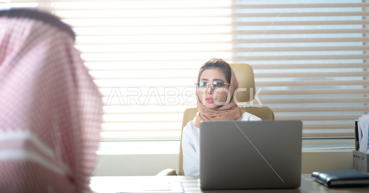 A Saudi Arabian Gulf doctor wearing a medical coat and sitting in front ...