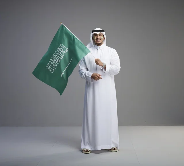 رجل سعودي بالزي التقليدي يحمل العلم الوطني في الاستوديو - صورة