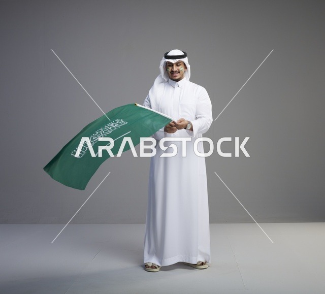 رجل سعودي بالزي التقليدي يحمل العلم الوطني في الاستوديو - صورة