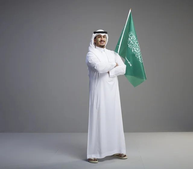 رجل سعودي بالزي التقليدي يحمل العلم الوطني في الاستوديو - صورة
