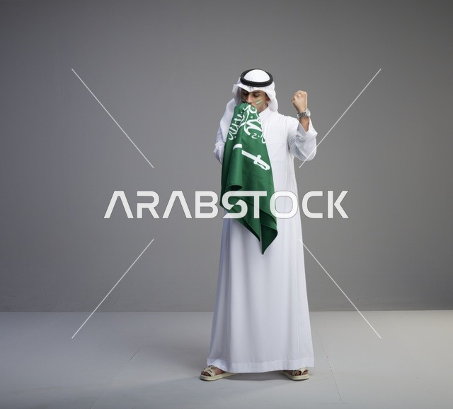 Saudi Man Kissing Saudi Arabia Flag on Grey Background - Photo