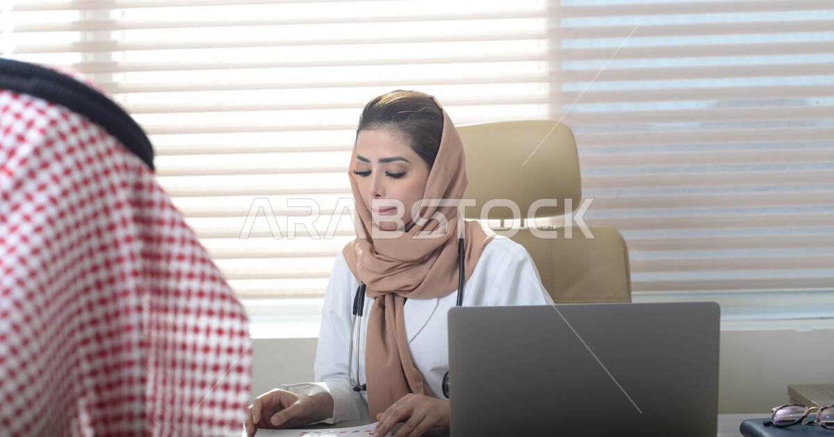 A Saudi Arabian Gulf doctor wearing a medical coat and sitting in her ...