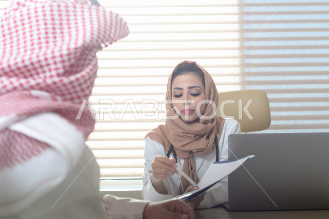 A Saudi Arabian Gulf doctor wearing a medical coat and sitting in her ...