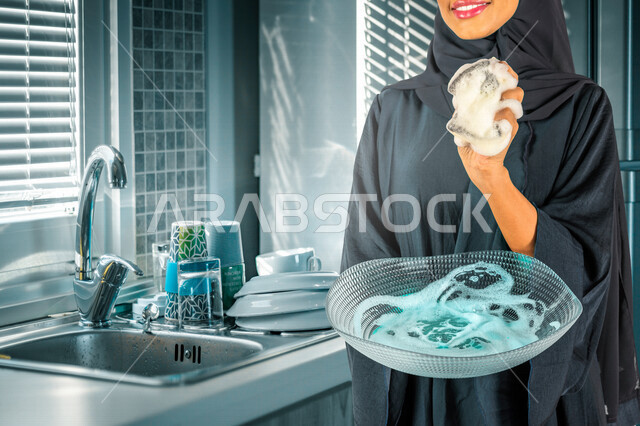 Close-up of a Saudi Arabian Gulf woman, washing dishes with a sponge in ...