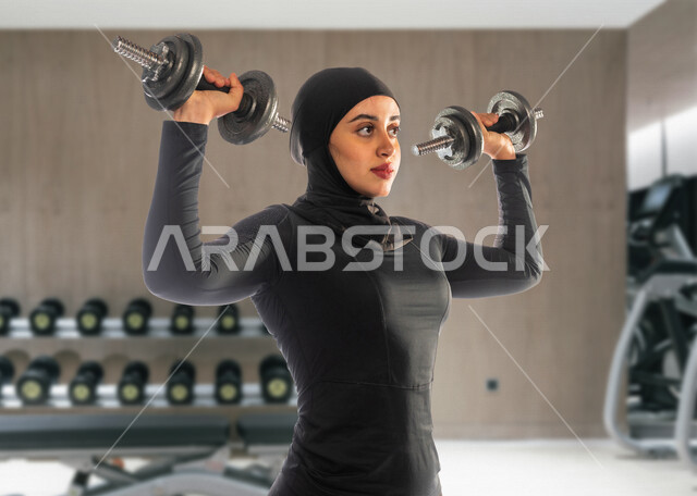 A veiled Saudi Arab girl in the gym with sports clothes, exercising ...