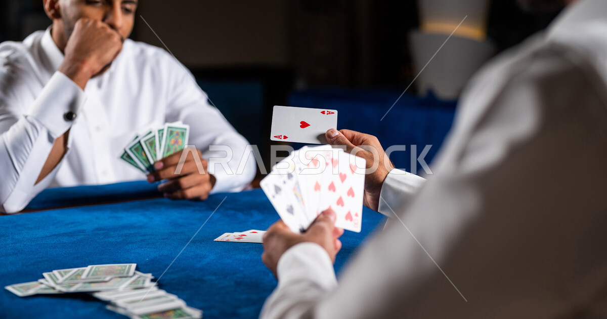 A close-up of two Saudi Arabian Gulf youths playing a game of cards ...