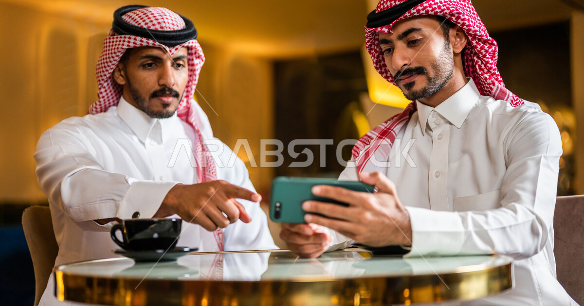 Two smiling Saudi Arabian Gulf men sitting in the cafe, enjoying ...