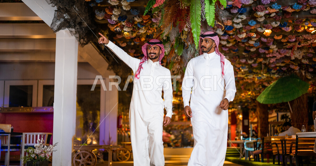 Two smiling Saudi Arabian Gulf Arab men are walking together on a ...