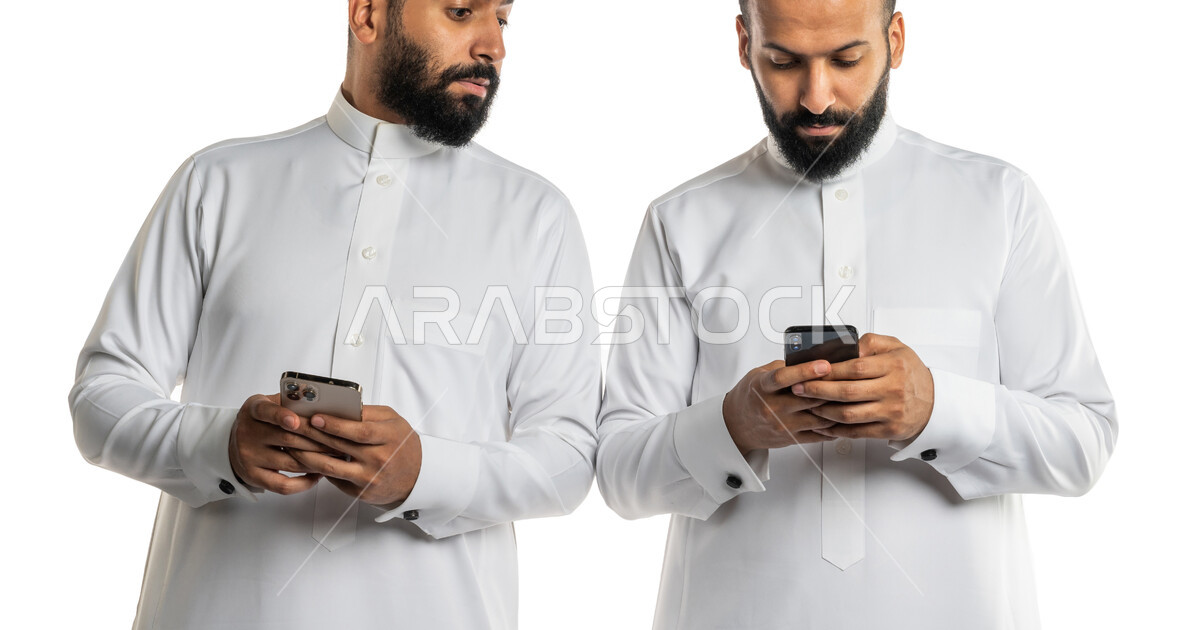 Portrait of two Saudi Arabian Gulf twin men using a mobile phone ...
