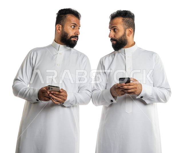 Portrait of two Saudi Arabian Gulf twin men using a mobile phone, using ...