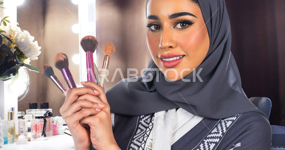 A veiled Saudi Arabian Gulf woman, carrying a set of makeup brushes ...