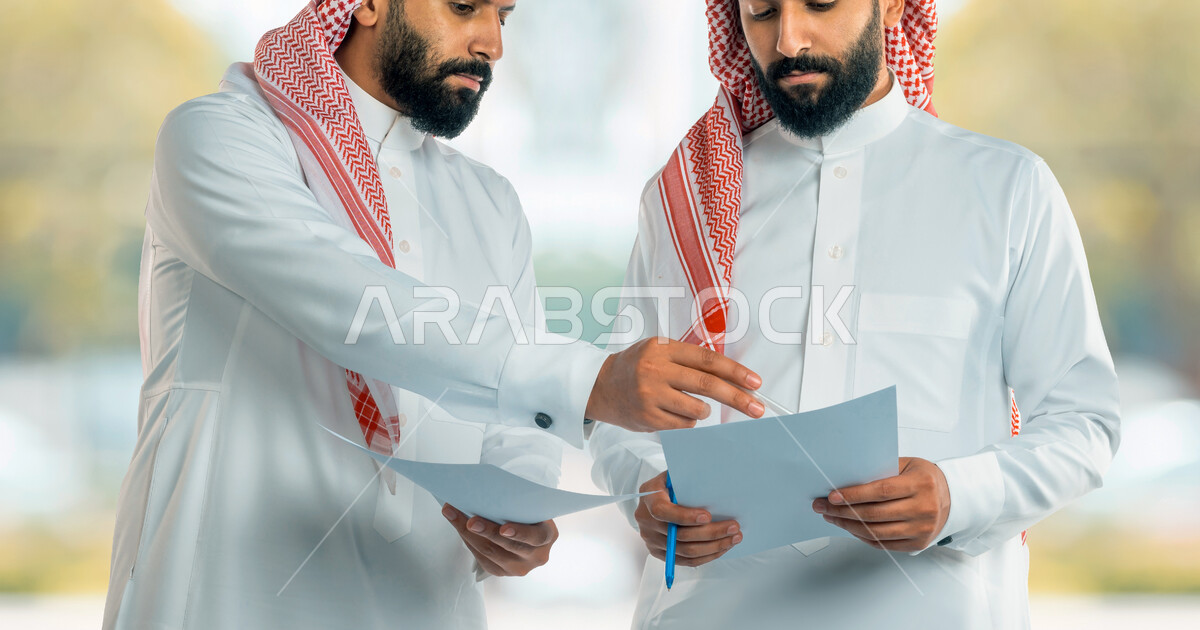 Two Saudi Arabian Gulf twin men holding work papers, work discussion ...
