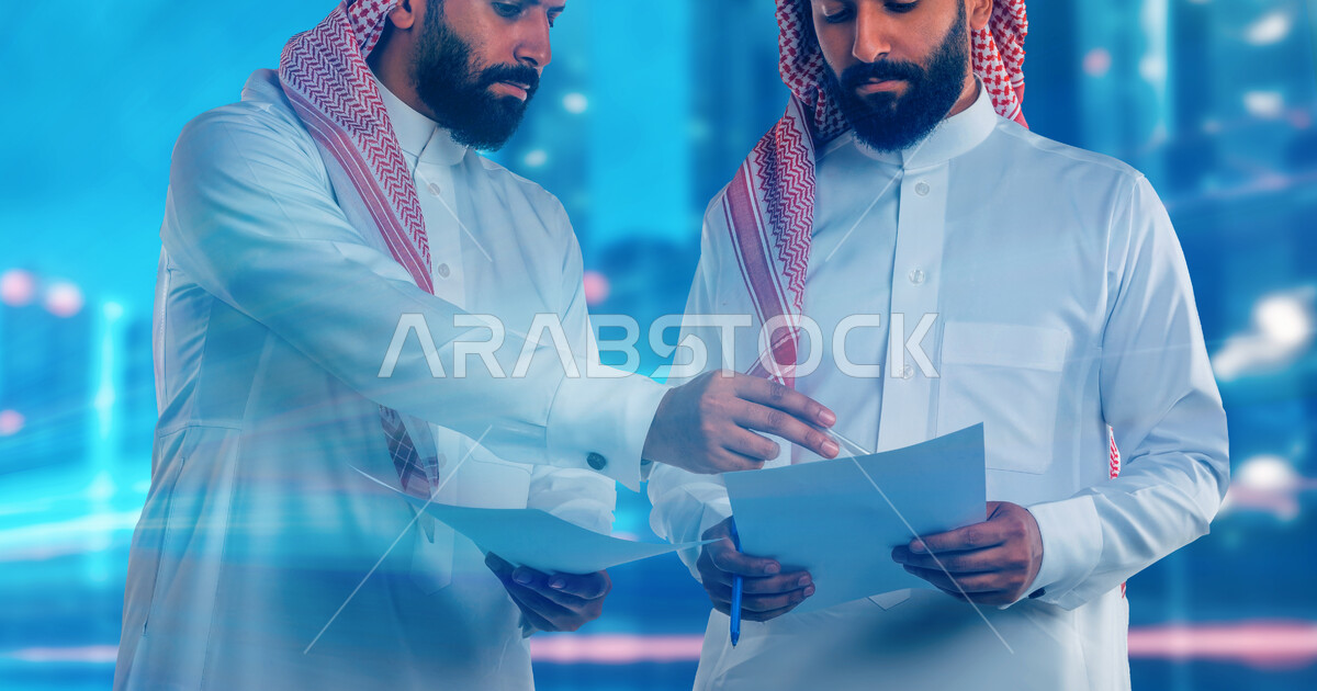 Two Saudi Arabian Gulf twin men holding work papers, work discussion ...
