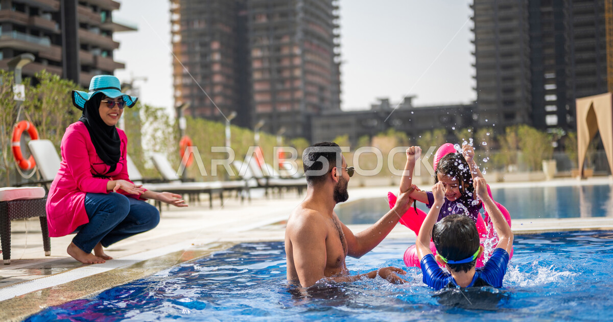 A Saudi Arabian Gulf family enjoying swimming in the water pool, a ...