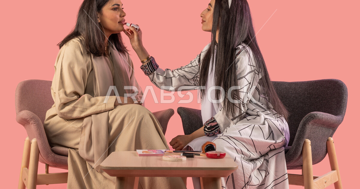 Portrait of two Saudi Arabian Gulf women, a young Saudi woman applying ...