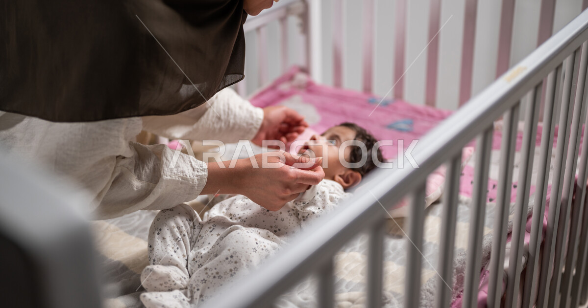 A Saudi Arabian Gulf mother with her infant child lying in the cradle ...