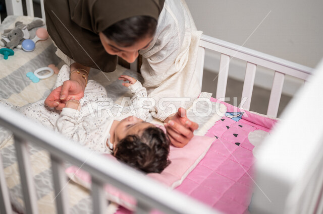 A Saudi Arabian Gulf mother with her infant child lying in the cradle ...