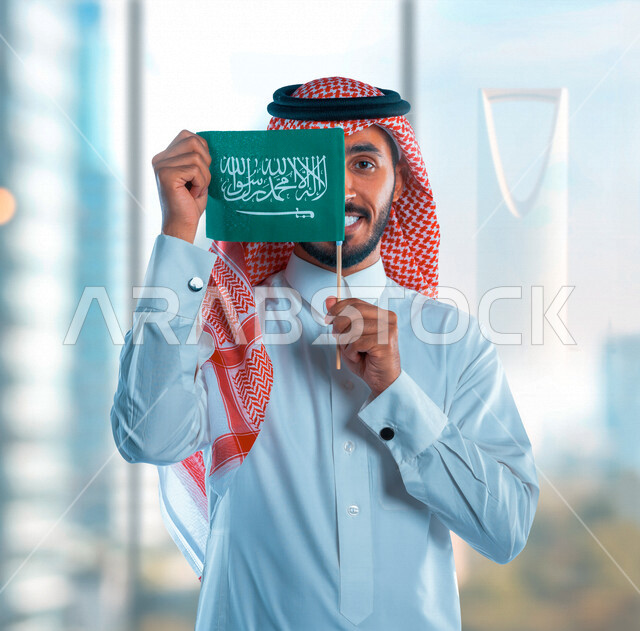 A Saudi Arabian Gulf man wearing a Saudi dress holds the flag of the ...