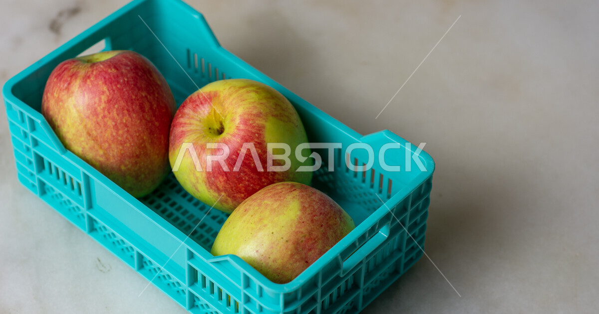 Close-up of apple fruit inside a plastic box on a white marble ...