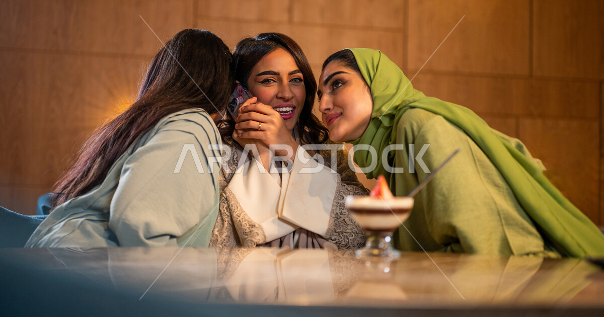 Saudi Arabian Gulf female friends sitting in the café, making a phone ...