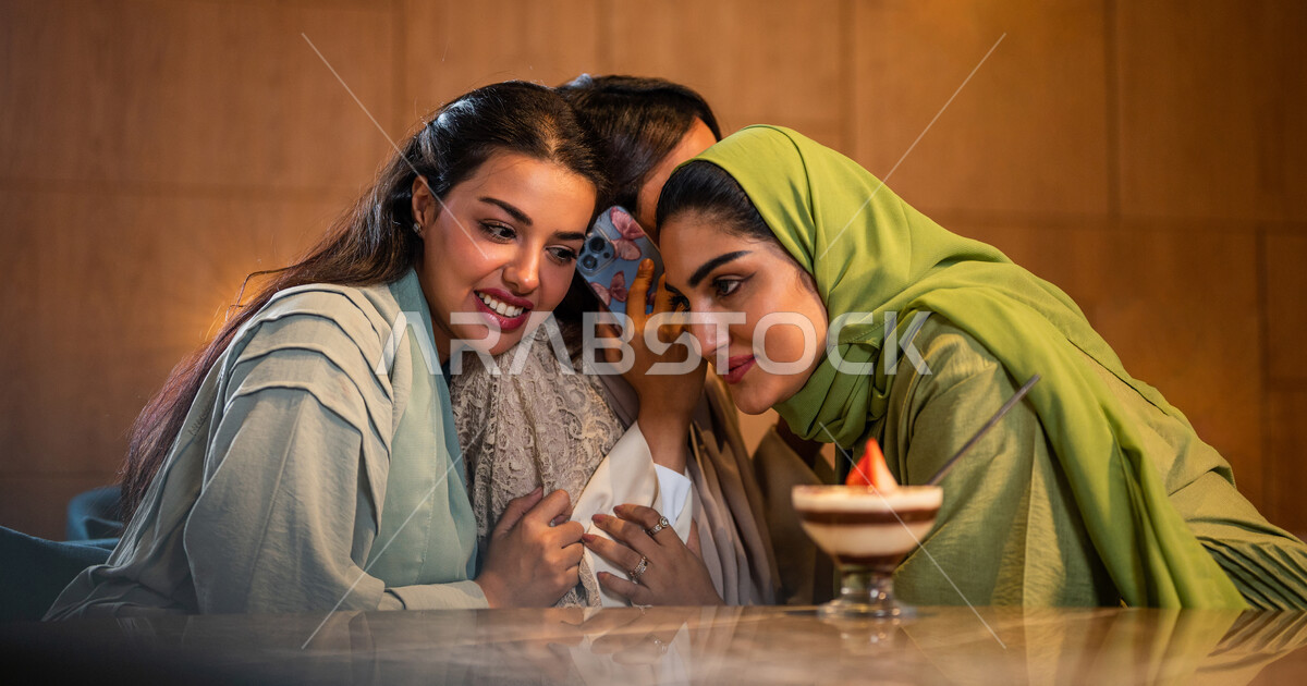 Saudi Arabian Gulf female friends sitting in the café, making a phone ...