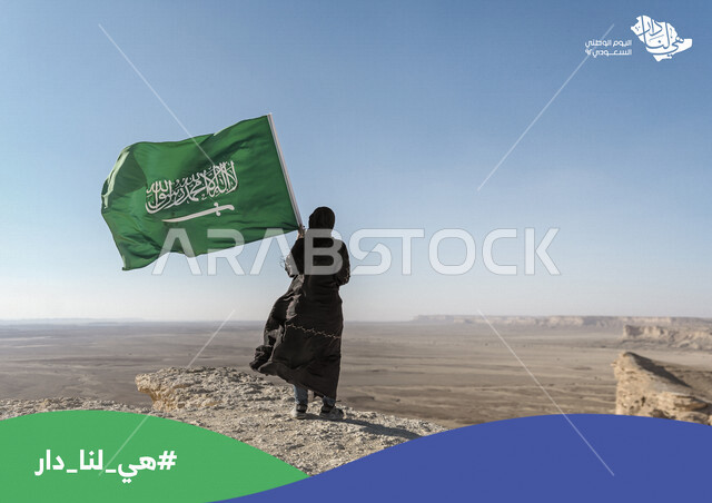 A corner from the back of a Saudi Arabian Gulf woman carrying the flag ...