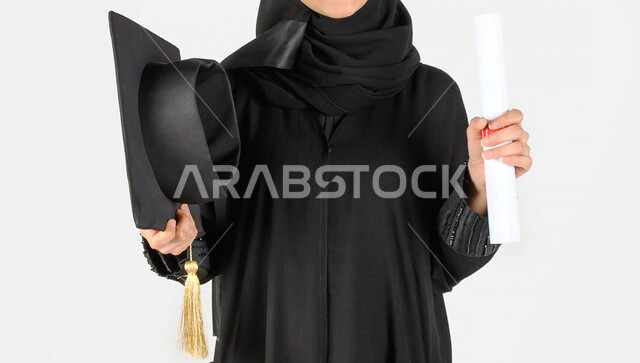 Portrait of a Saudi Arabian Gulf student wearing a black abaya holding a hat and graduation ...