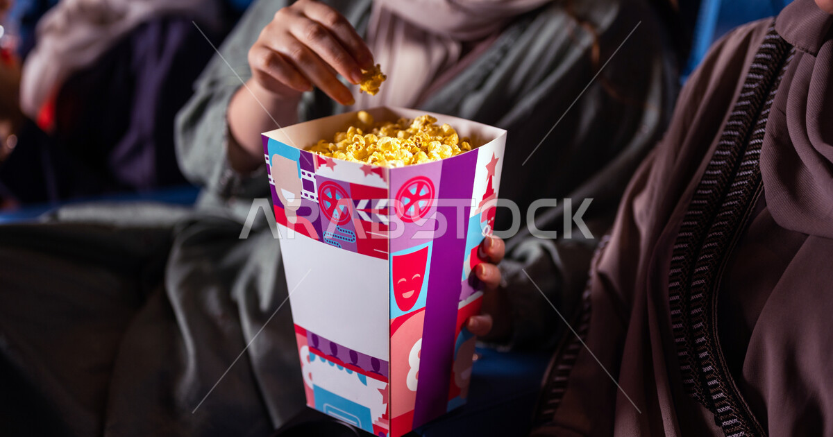 Saudi Gulf Arab female friends sitting in the cinema, enjoying eating ...