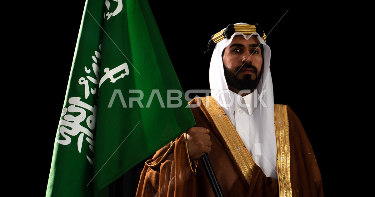 Portrait of a Saudi Arabian Gulf man raising the Saudi flag, wearing ...