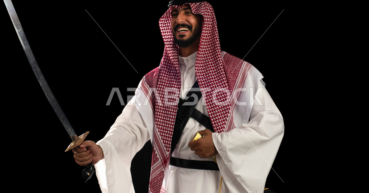 A Saudi Arabian Gulf man, holding a long sword in his hand, wears the ...