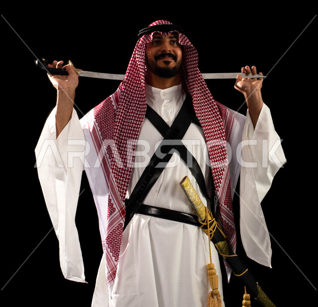 A Saudi Arabian Gulf man, holding a long sword in his hand, wears the ...