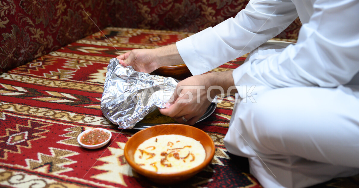 A Saudi Arabian Gulf man at the dining table, eating by hand, sitting ...