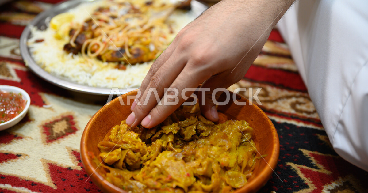 A Saudi Arabian Gulf man at the dining table, eating by hand, sitting ...