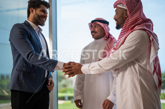 A Saudi Arabian Gulf businessman in a Saudi dress shakes hands with an ...