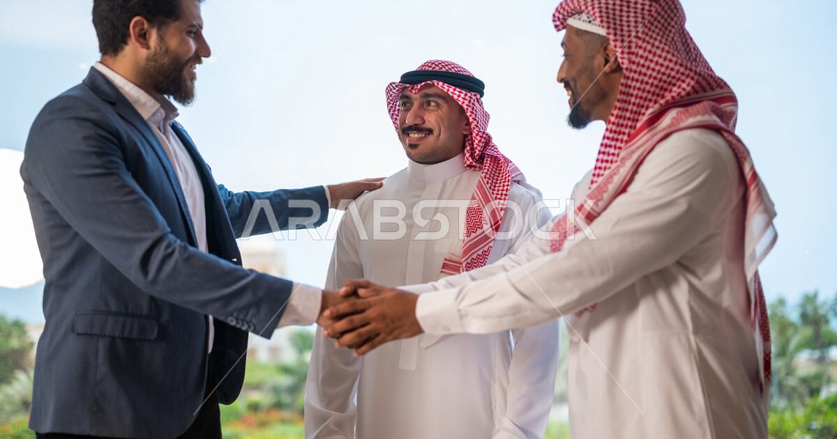 A Saudi Arabian Gulf businessman in a Saudi dress shakes hands with an ...