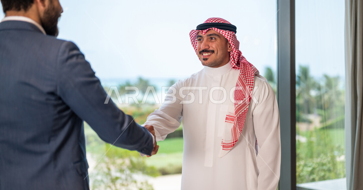 A Saudi Arabian Gulf businessman in a Saudi dress shakes hands with an ...